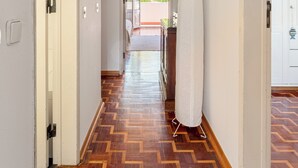 Um corredor com piso de madeira em padrão herringbone, paredes brancas e luminária no teto.
