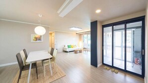 Uma sala de estar ampla com uma mesa de jantar, cadeiras, um sofá e um grande painel de vidro deslizante que dá para uma área externa.