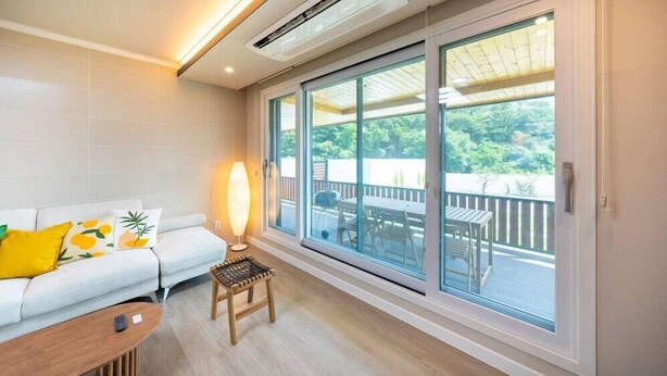 Quarto moderno com sofá, mesinha, banco e uma grande porta de vidro deslizante para um pátio externo com mesa e cadeiras.