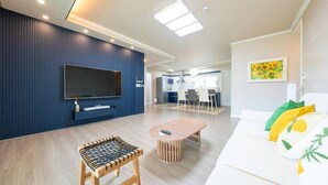 Uma sala de estar moderna com televisão de tela plana, um banco de madeira, uma mesa de centro redonda e um sofá branco com almofadas coloridas.