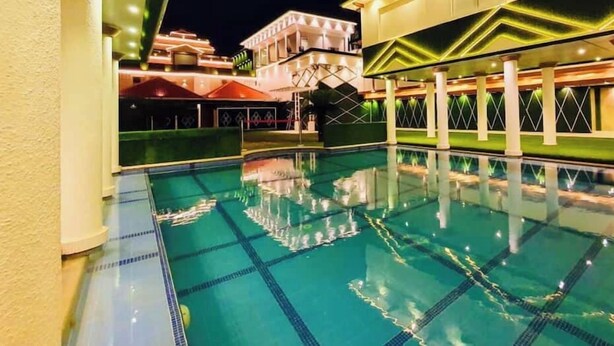 Uma piscina com água cristalina, rodeada por um edifício de design moderno e uma área coberta ao fundo.