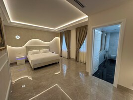 Quarto moderno com uma cama grande, mesa de cabeceira e banheiro visível através de uma porta aberta.