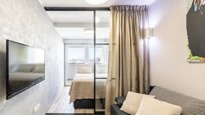 Quarto moderno com cama, televisão, sof á e vista da cidade através de amplas janelas.