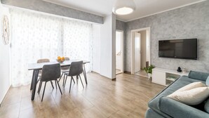 Uma sala de estar moderna com área de jantar, um sofá cinza, uma TV de tela plana e um console branco.