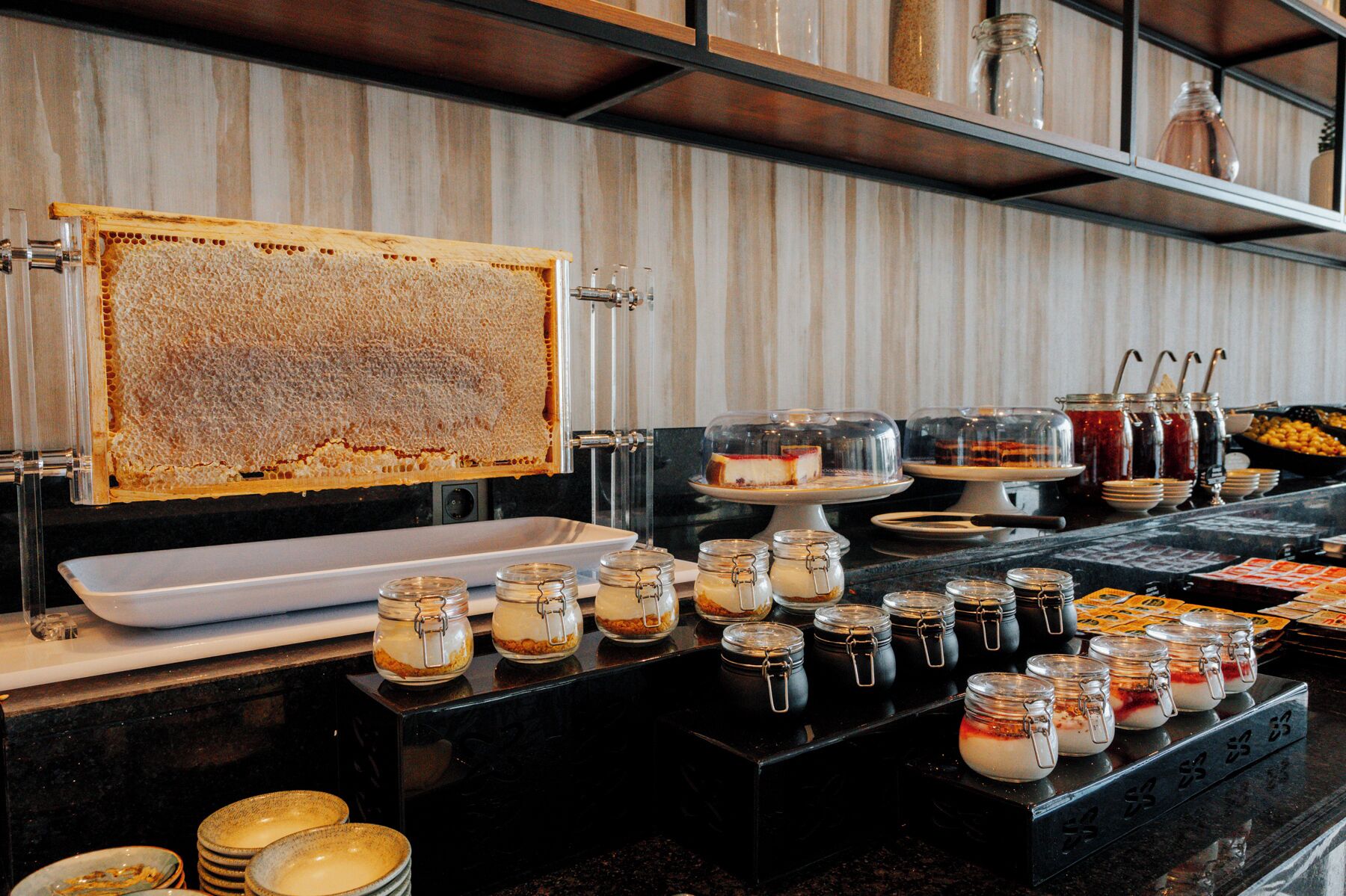 Disposição de buffet com um pegador de mel em formato de favo, diversos doces e alimentos em potes.