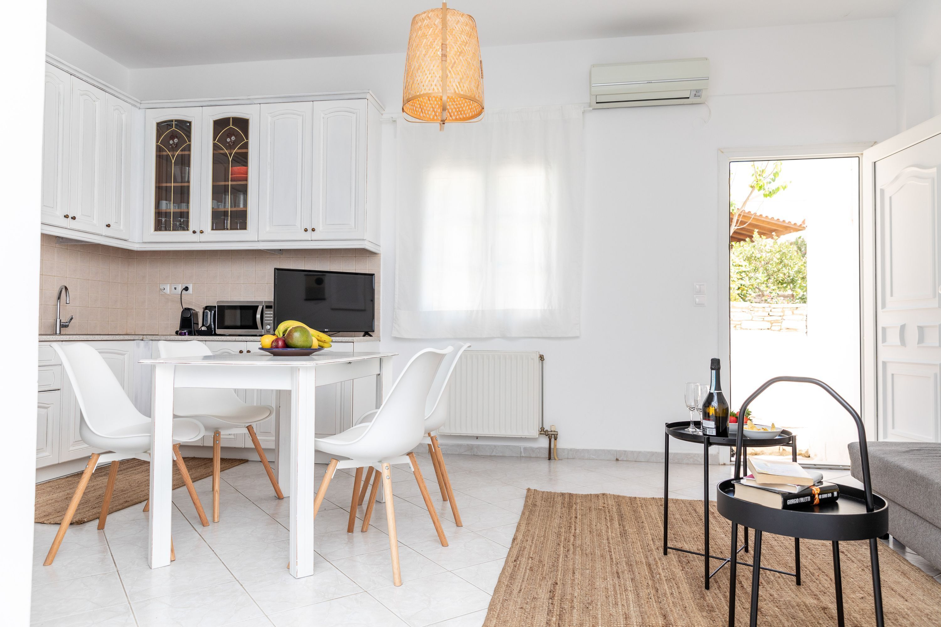 Cozinha moderna com armários brancos, uma mesa de jantar com cadeiras, um lustre pendurado e vista para o exterior pela janela.