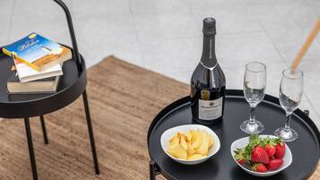 Uma mesa com uma garrafa de champanhe, duas taças, um recipiente com batatas fritas, um recipiente com morangos e um livro.