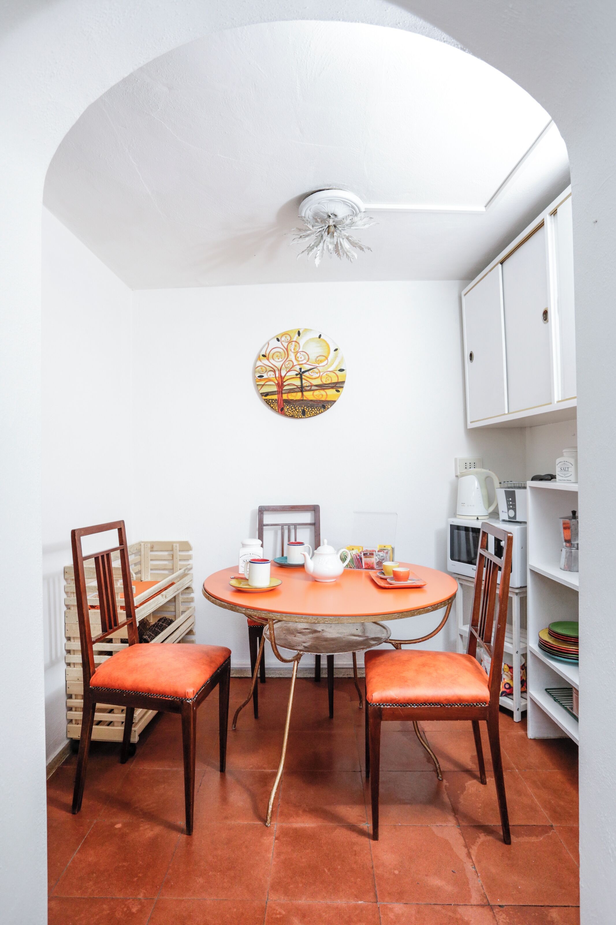 Uma cozinha compacta com uma mesa redonda, duas cadeiras, um ventilador de teto e um relógio fixado na parede.