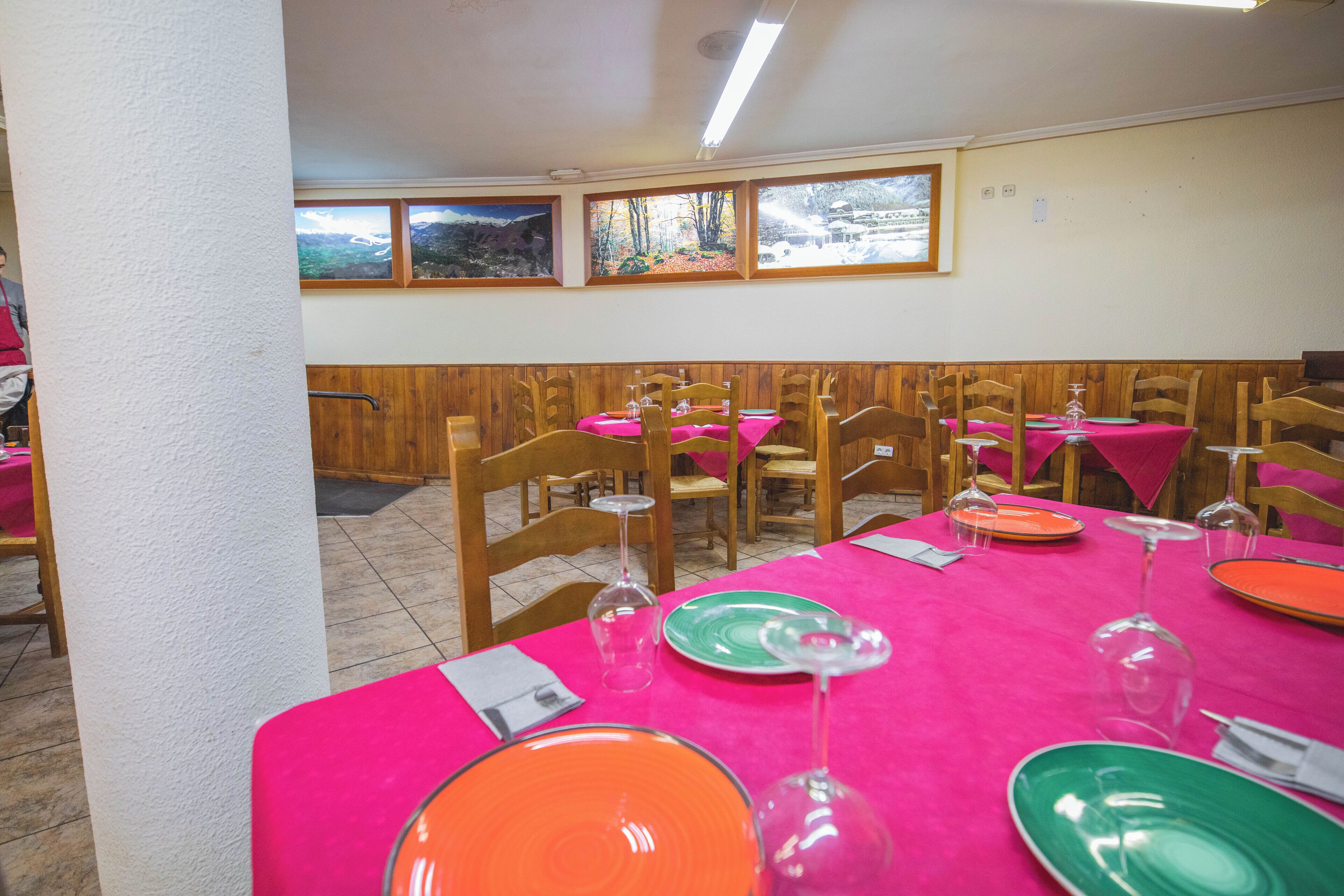 Uma área de refeições com cadeiras e mesas de madeira, cada uma com toalha de mesa rosa e copos de vinho.