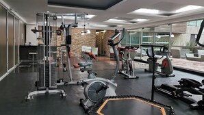 Uma academia moderna com diversos equipamentos de exercício, uma parede de pedra e amplas janelas com vista para o exterior.