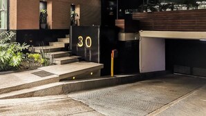 Entrada de um edifício moderno com placa indicando o número 30, degraus de concreto e uma pequena área ajardinada.