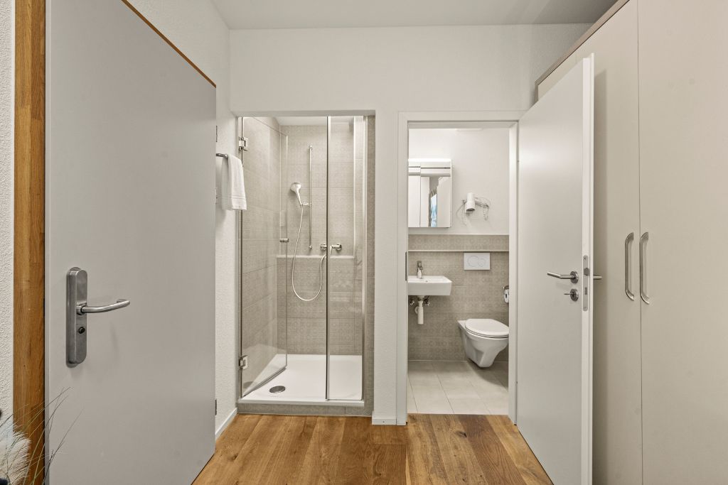 Uma casa de banho moderna com chuveiro, sanita e lavatório.