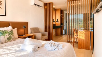 Quarto de hotel moderno com cama, poltrona, escrivaninha e vista para o exterior.