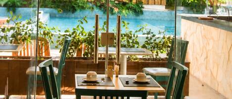Restaurante com vista para uma piscina e vegetação, com mesas e cadeiras.