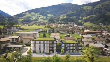 Zona residencial com casas modernas, um edifício central com varandas e montanhas ao fundo.