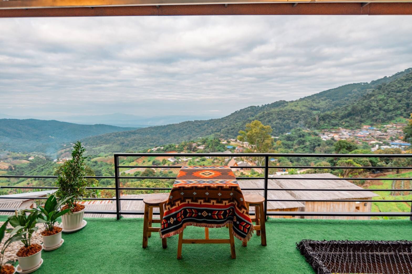 Uma varanda com mesa e cadeiras, vista para uma paisagem montanhosa e plantas em vasos.