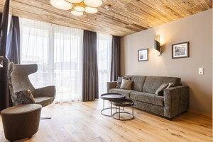 Uma sala de estar moderna com teto de madeira, um sofá cinza, uma cadeira única e uma mesa de centro redonda.