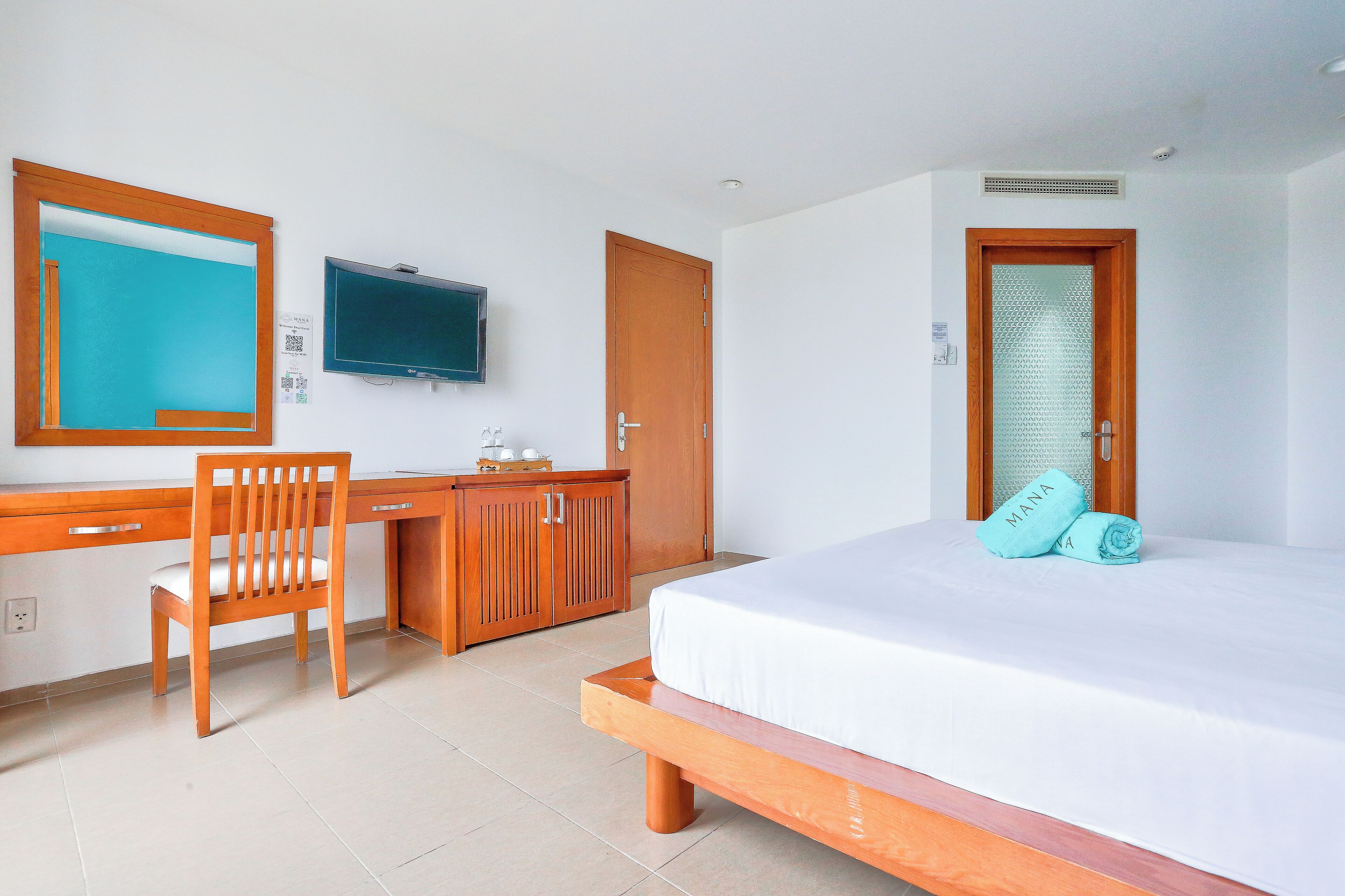 Quarto de hotel com uma cama, escrivaninha, cadeira, televisão e guarda-roupa.