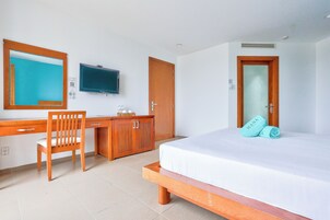 Quarto de hotel com uma cama, escrivaninha, cadeira, televisão e guarda-roupa.