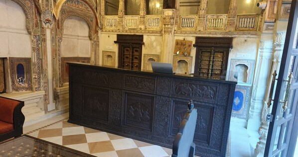 Um balcão de recepção ricamente decorado, com detalhes de escultura elaborados, piso xadrez e elementos arquitetônicos clássicos.