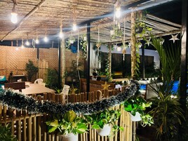 Uma área externa com mesas e cadeiras, cercada por cercas de bambu e plantas em vasos.
