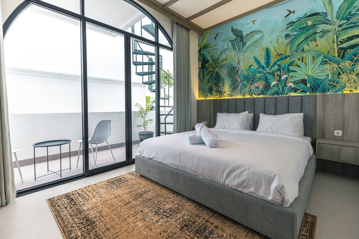 Quarto moderno com uma cama grande, um mural tropical, uma escada e uma varanda com cadeiras.