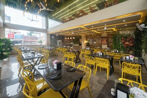 Restaurante com cadeiras e mesas amarelas, ventiladores de teto e plantas dentro.