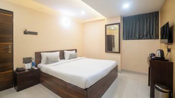 Quarto de hotel com cama de madeira, mesa de cabeceira com telefone e garrafa, televisão na parede e lixeira.