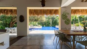 Um interior moderno com vista para a piscina, uma área de refeições e um jardim tropical lá fora.