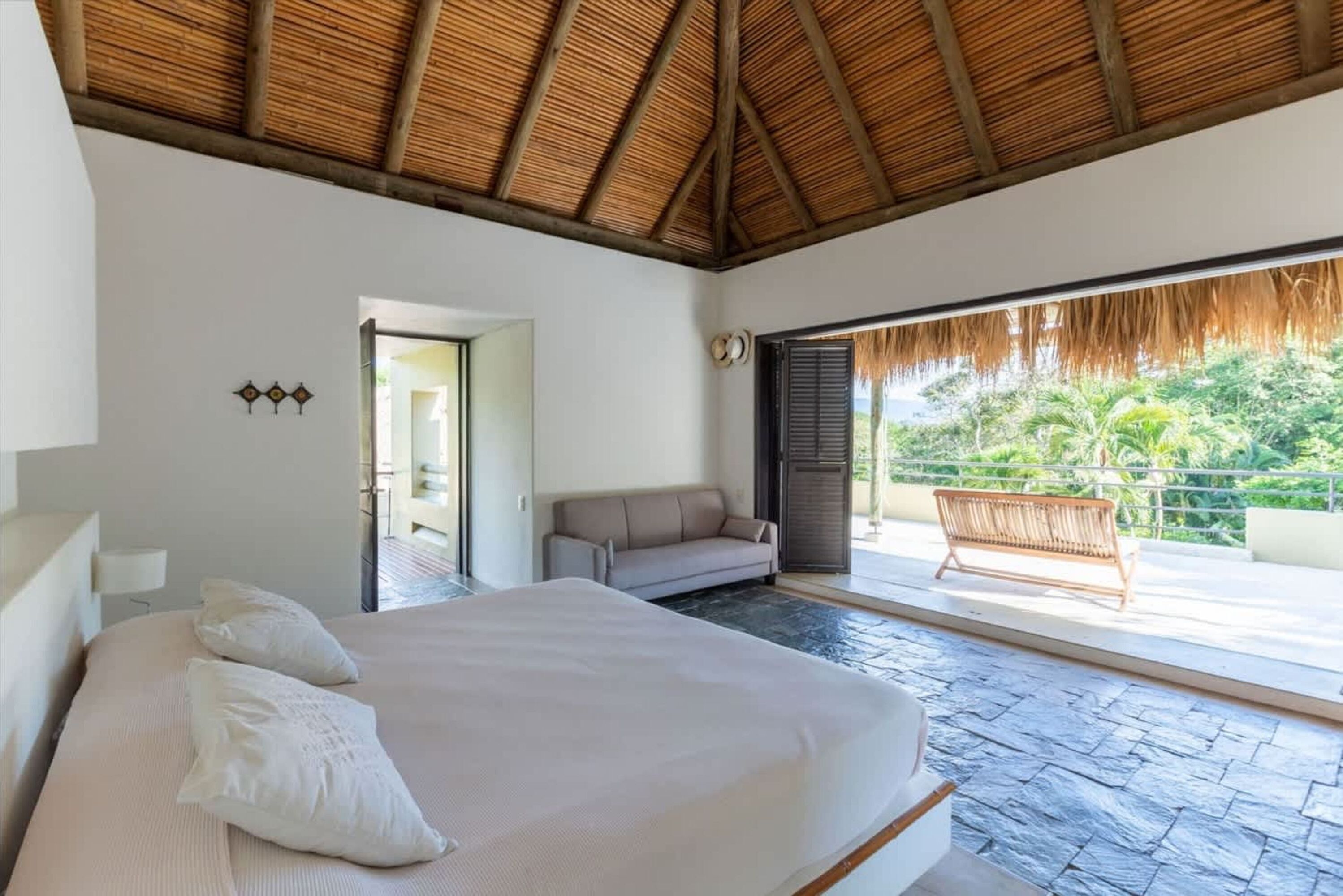 Quarto com cama, sofá e varanda com vista para vegetação.