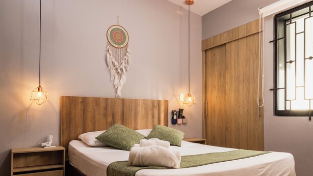 Cama bem arrumada com almofadas verdes e brancas, cabeceira de madeira e um sonhoapanhado na parede.