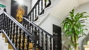 Uma escada com balaústres pretos e um corrimão de madeira, uma estátua de Buda na parede e um vaso de planta.