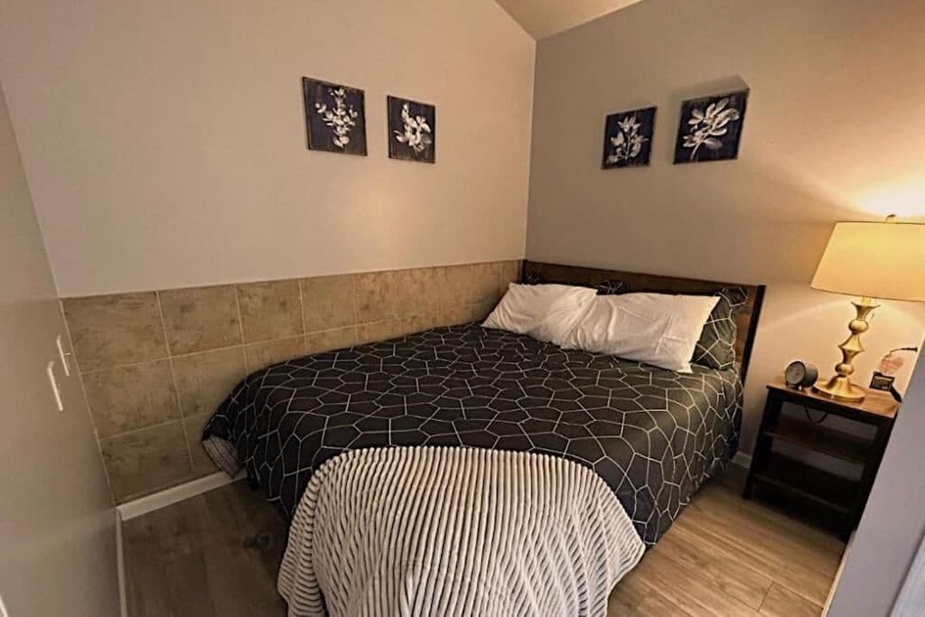 Quarto com cama, mesa de cabeceira e luminária na parede.
