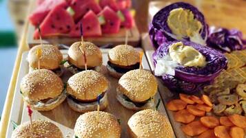 Uma mesa de buffet com mini sanduíches, fatias de melancia, uma salada com repolho roxo e palitos de cenoura.