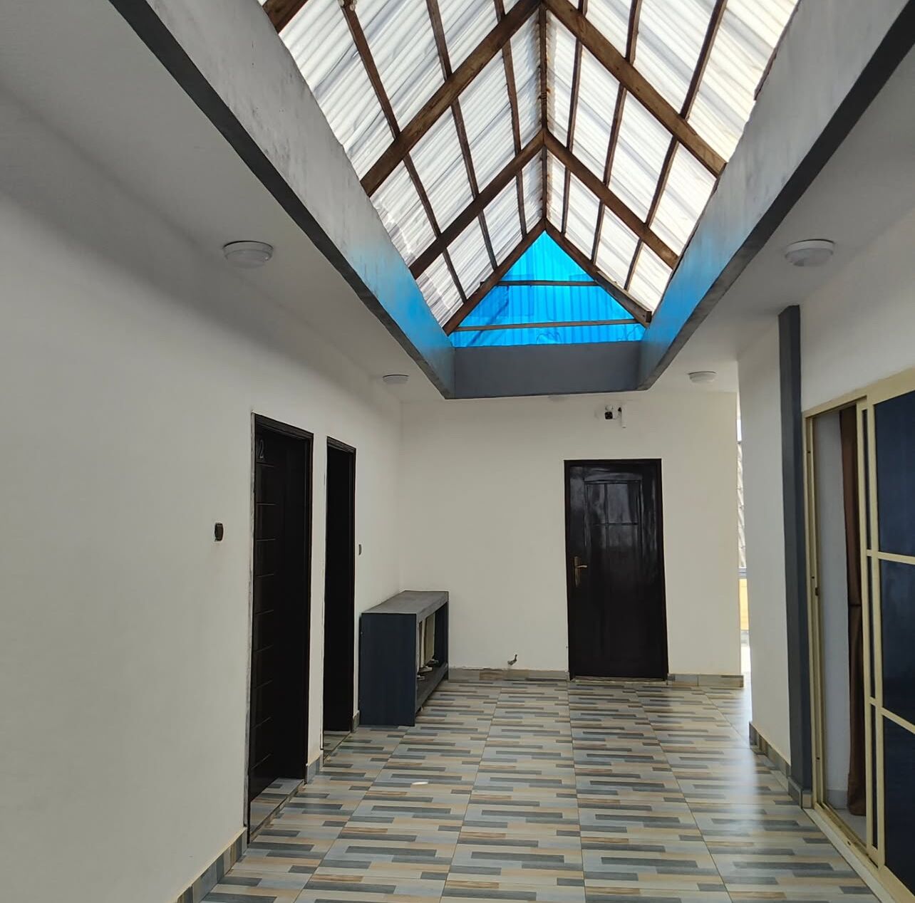 Um corredor com claraboia, piso ladrilhado e portas pretas.