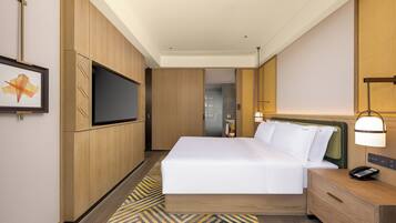 Quarto de hotel com cama, mesa de cabeceira, abajur e televisão de tela plana na parede.