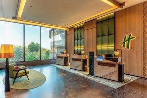 Um espaço de recepção de hotel com design moderno, incluindo um balcão de atendimento, área de estar e grandes janelas com vista para o exterior.