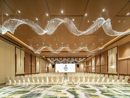 Sala de conferências com fileiras de cadeiras, uma tela grande na frente e luminárias no teto que lembram ondas.