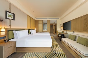 Quarto de hotel com uma cama grande, uma escrivaninha, um sofá e uma televisão.