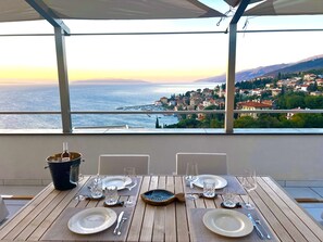 Mesa posta para dois, vista para o mar e uma cidade ao fundo.