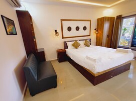 Quarto de hotel moderno com uma cama grande, um banco, uma mesa de cabeceira, ar condicionado fixado na parede e uma janela com cortinas.