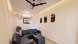 Uma sala de estar com sofá, mesa de centro, ventilador de teto, ar condicionado e obras de arte penduradas na parede.