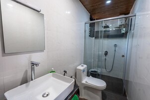 Casa de banho com lavatório branco, sanita e cabine de duche com parede de vidro.