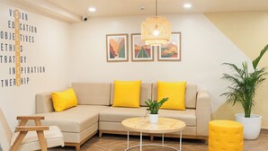 Sala de estar moderna com sofá, almofadas amarelas, mesa de centro redonda de madeira e luminária pendente.
