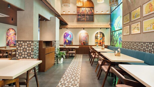 Interior de restaurante com várias mesas e cabines, piso estampado e obras de arte nas paredes.