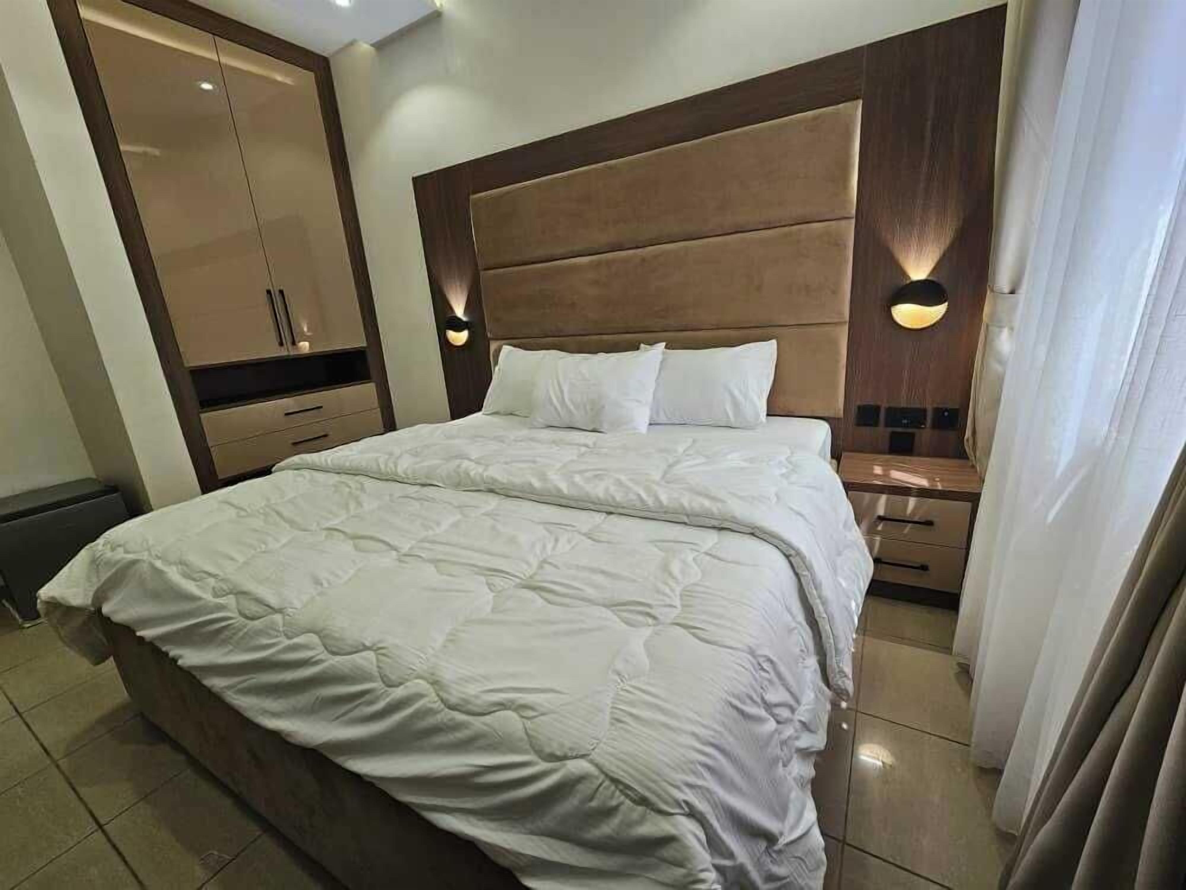 Quarto com cama grande, cabeceira de madeira, mesas de cabeceira e guarda-roupa.