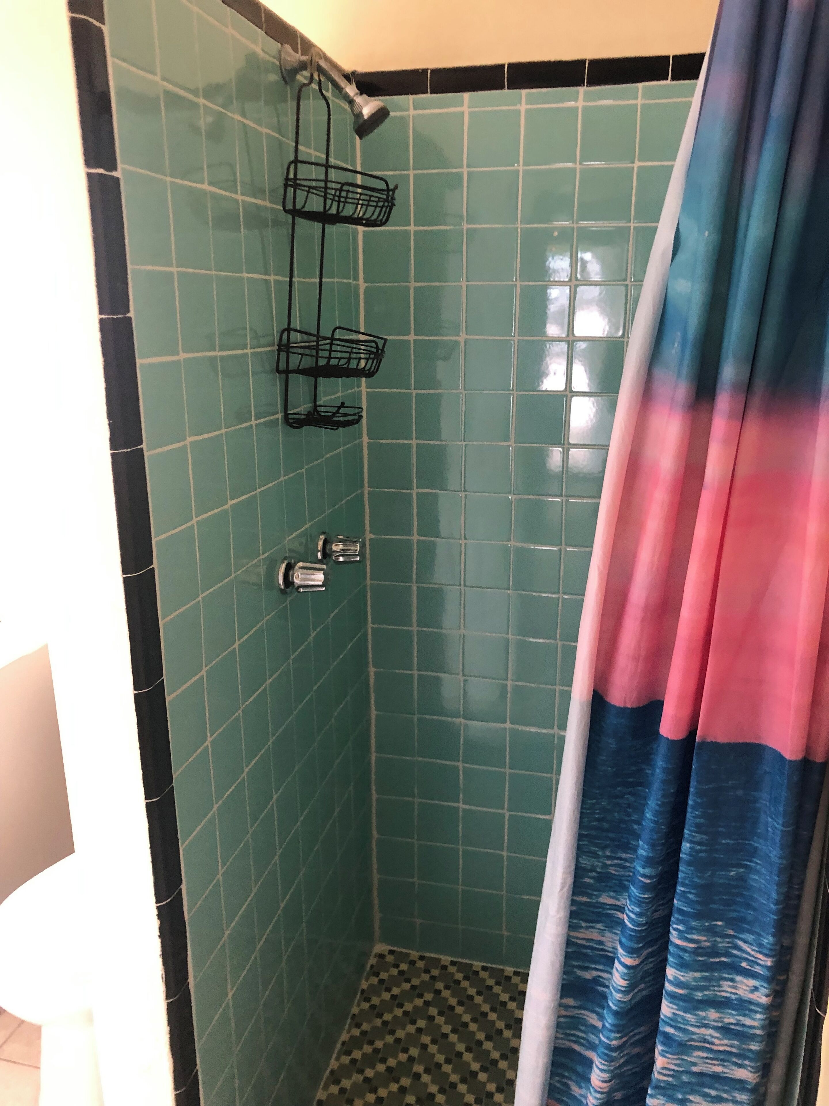 Um chuveiro pequeno com azulejos, cortina e um suporte de metal.