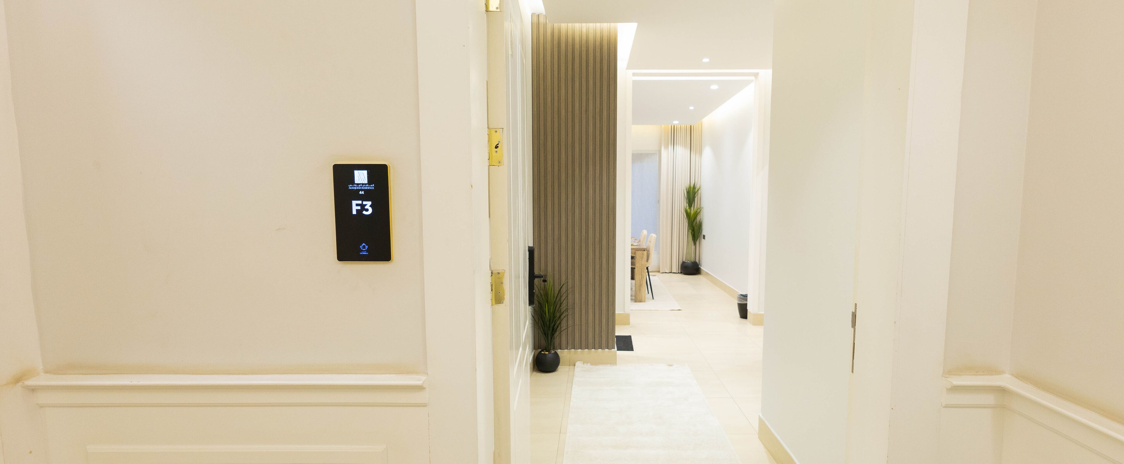 Corredor com placa indicando o quarto F3, um vaso de planta e uma porta no final.