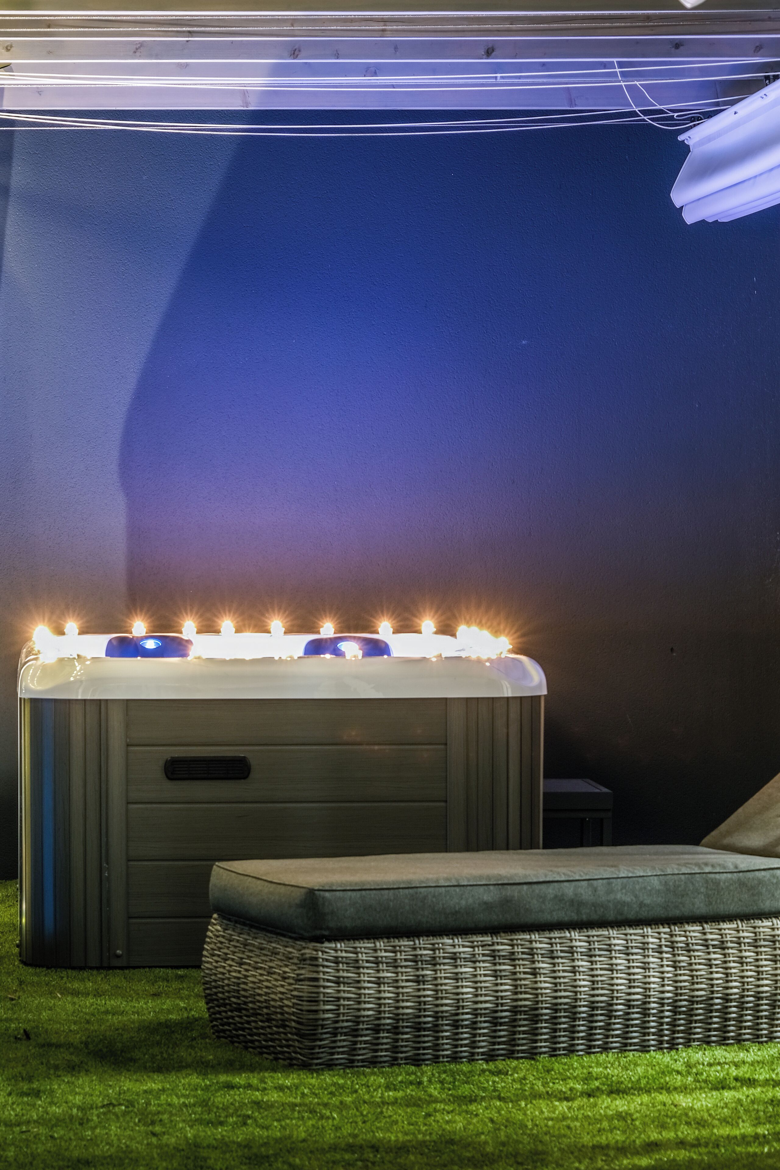 Uma banheira de hidromassagem com velas, um banquinho de vime e uma mesa pequena.