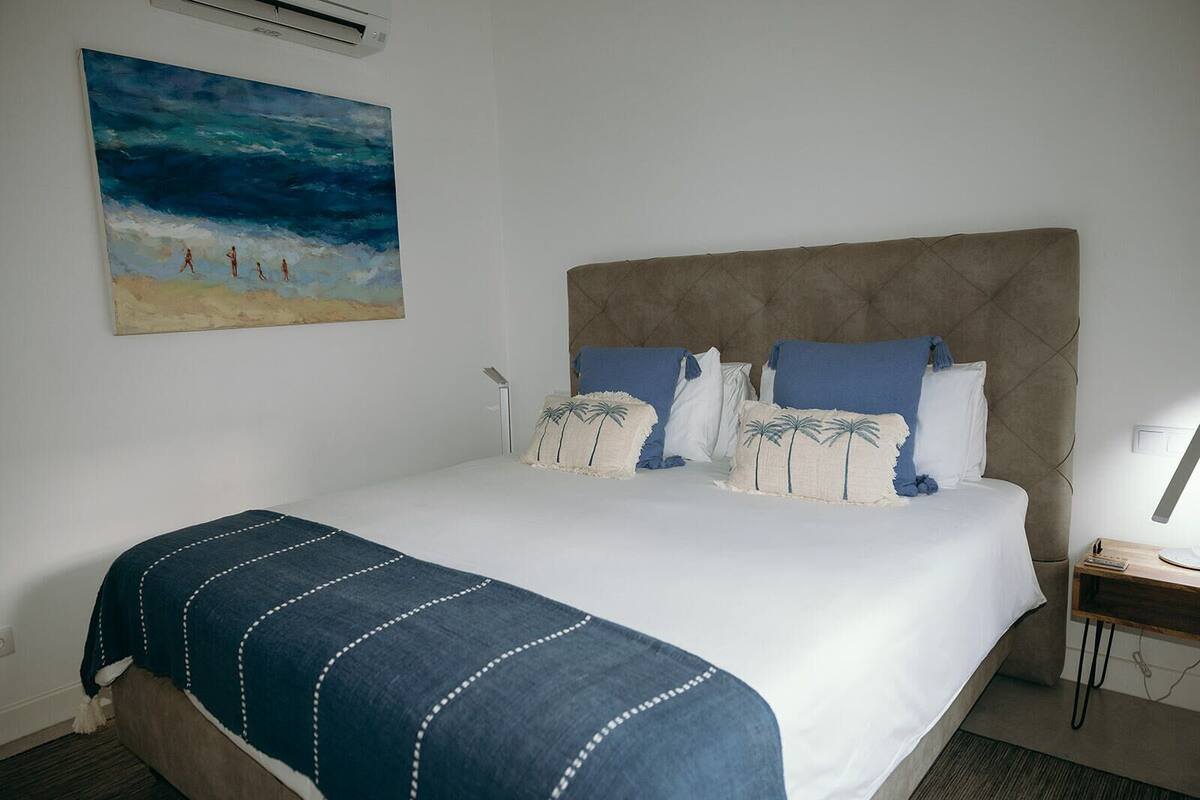 Quarto de hotel com uma cama grande, cabeceira e um quadro na parede.